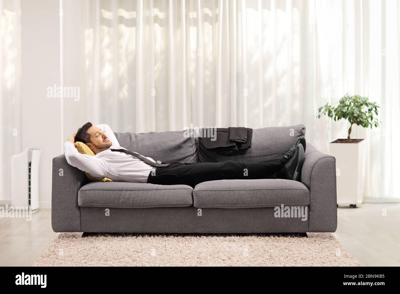 Businessman resting on a gray sofa at home in a living room Stock Photo ...
