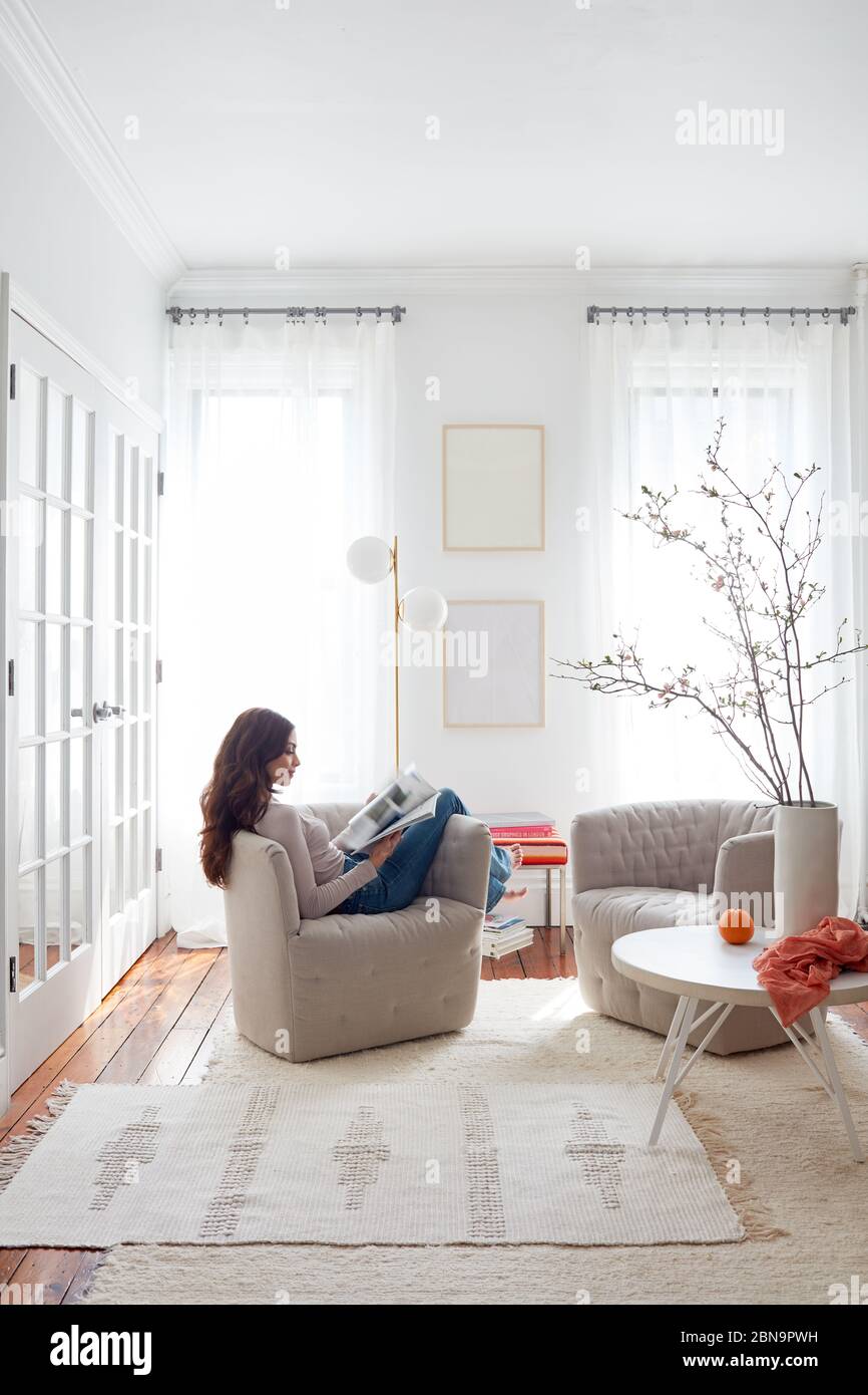 Woman reading in modern chair in bright, white living space Stock Photo ...