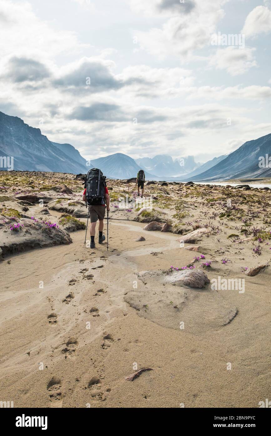 Rear view of two backpackers hiking, leaving footprints in the sand ...