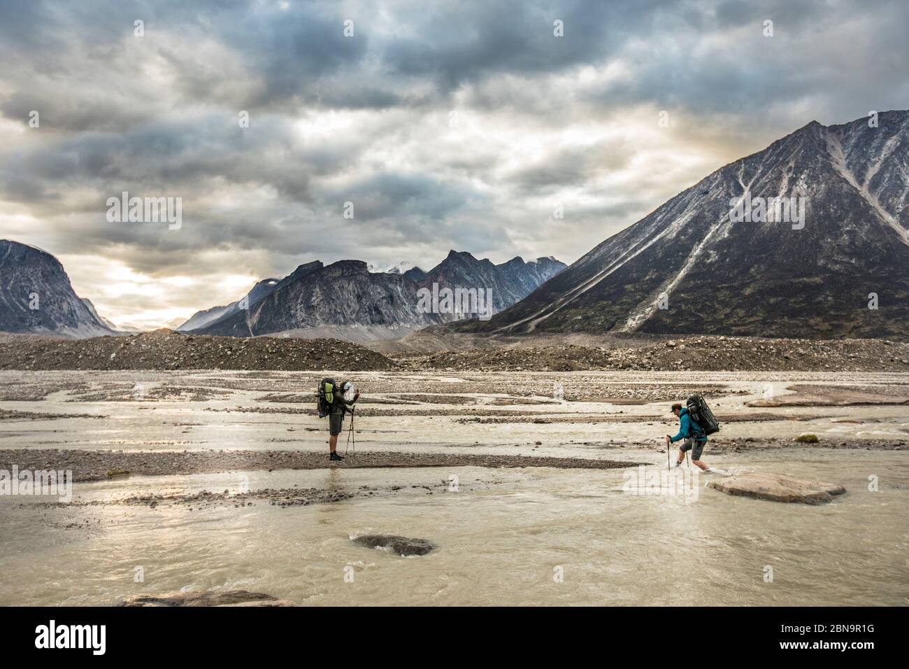 Two backpackers navigate crossing a braided river in a mountain pass ...