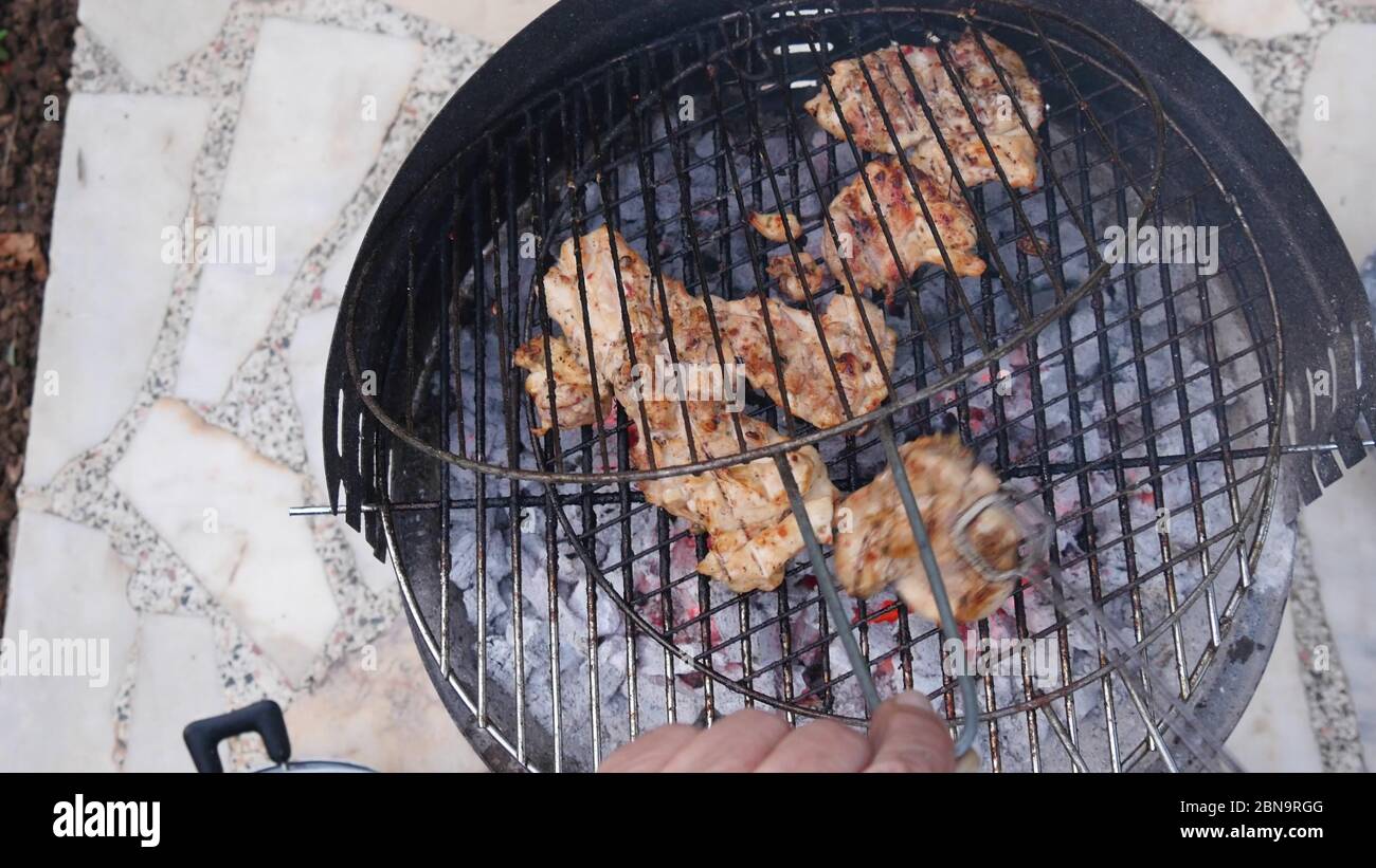 Man's hand using tongs For turning chicken meat on the barbecue grill ...