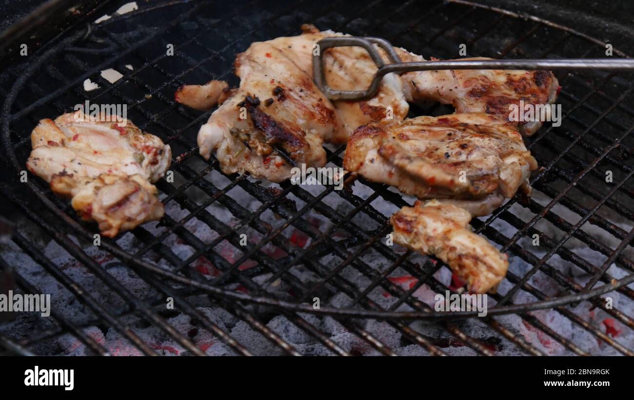 Man's hand using tongs For turning chicken meat on the barbecue grill ...