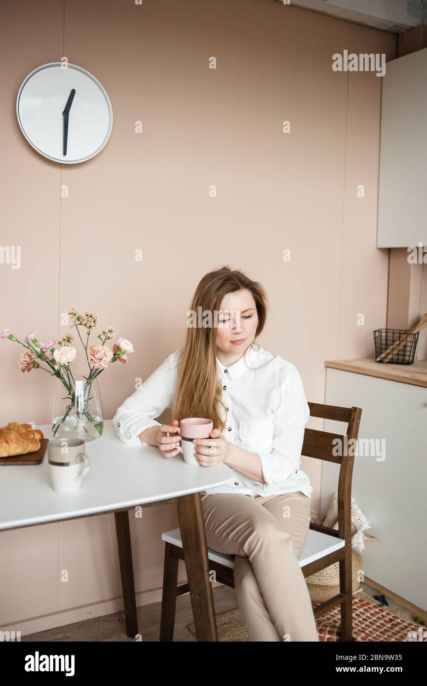 tired woman with disheveled hair and a lowered look sits in kitchen ...