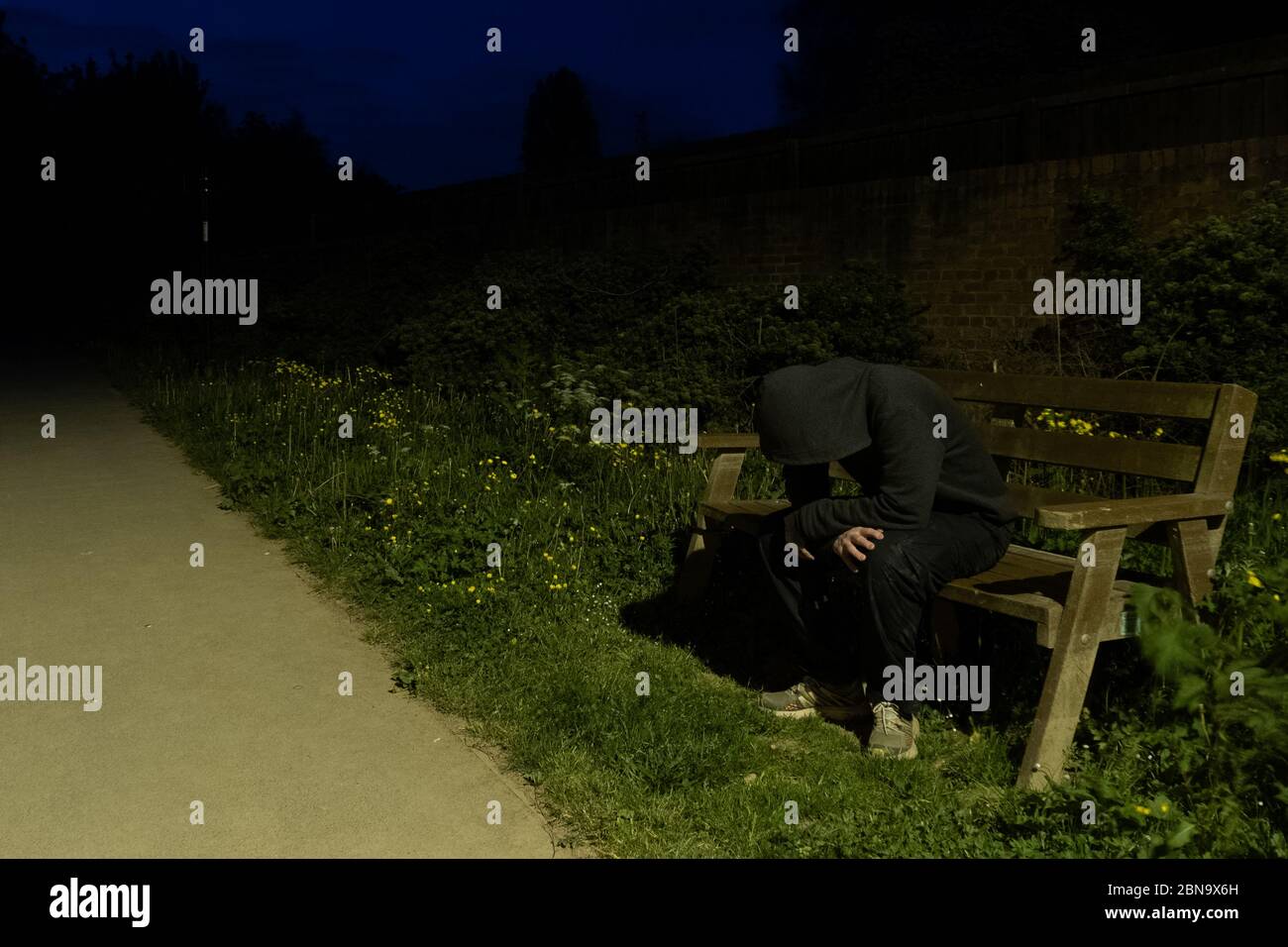 A mysterious hooded figure, head down. Sitting on a bench outside at ...
