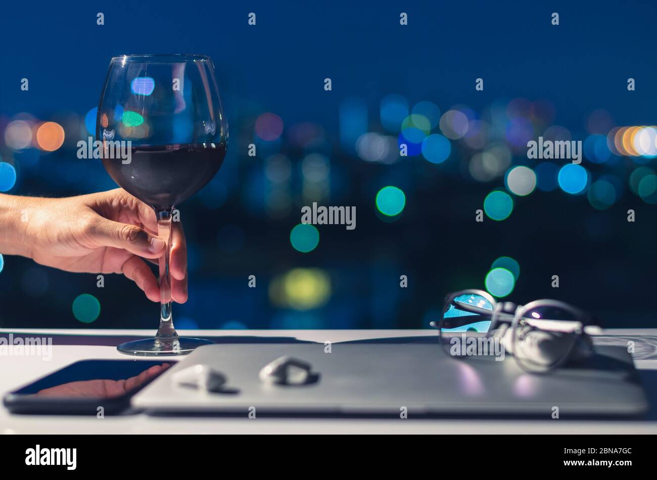 Hand holding a glass of red wine on table to enjoy the night after ...
