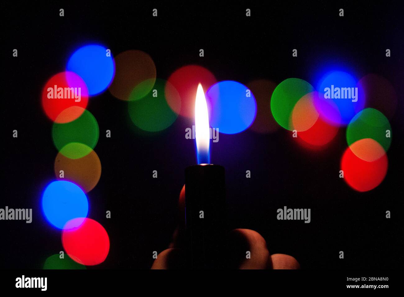 Closeup of a flame from a lighter against a dark background with bokeh ...