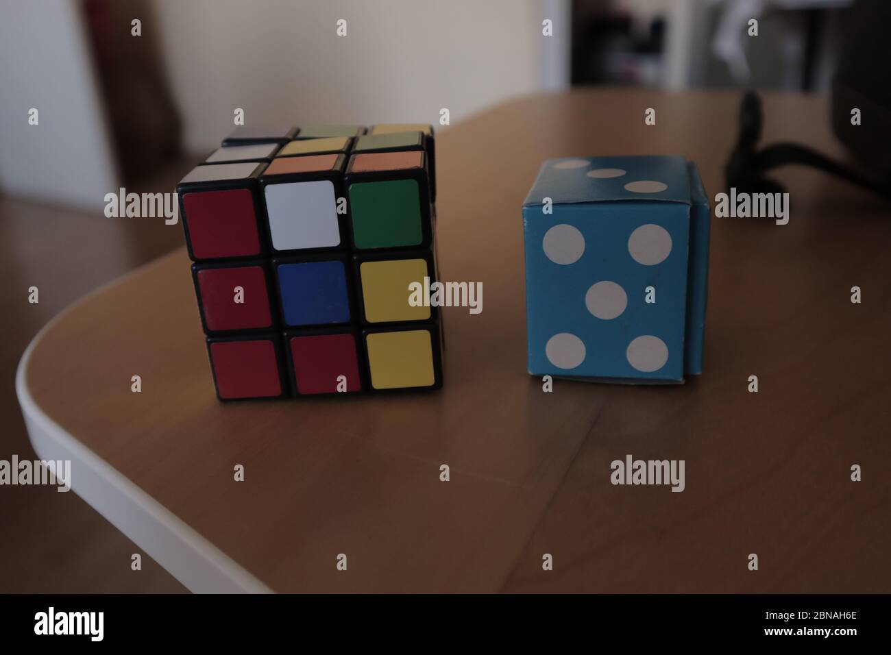 Selective shot of a Rubik's cube and dice on a wooden table and a ...