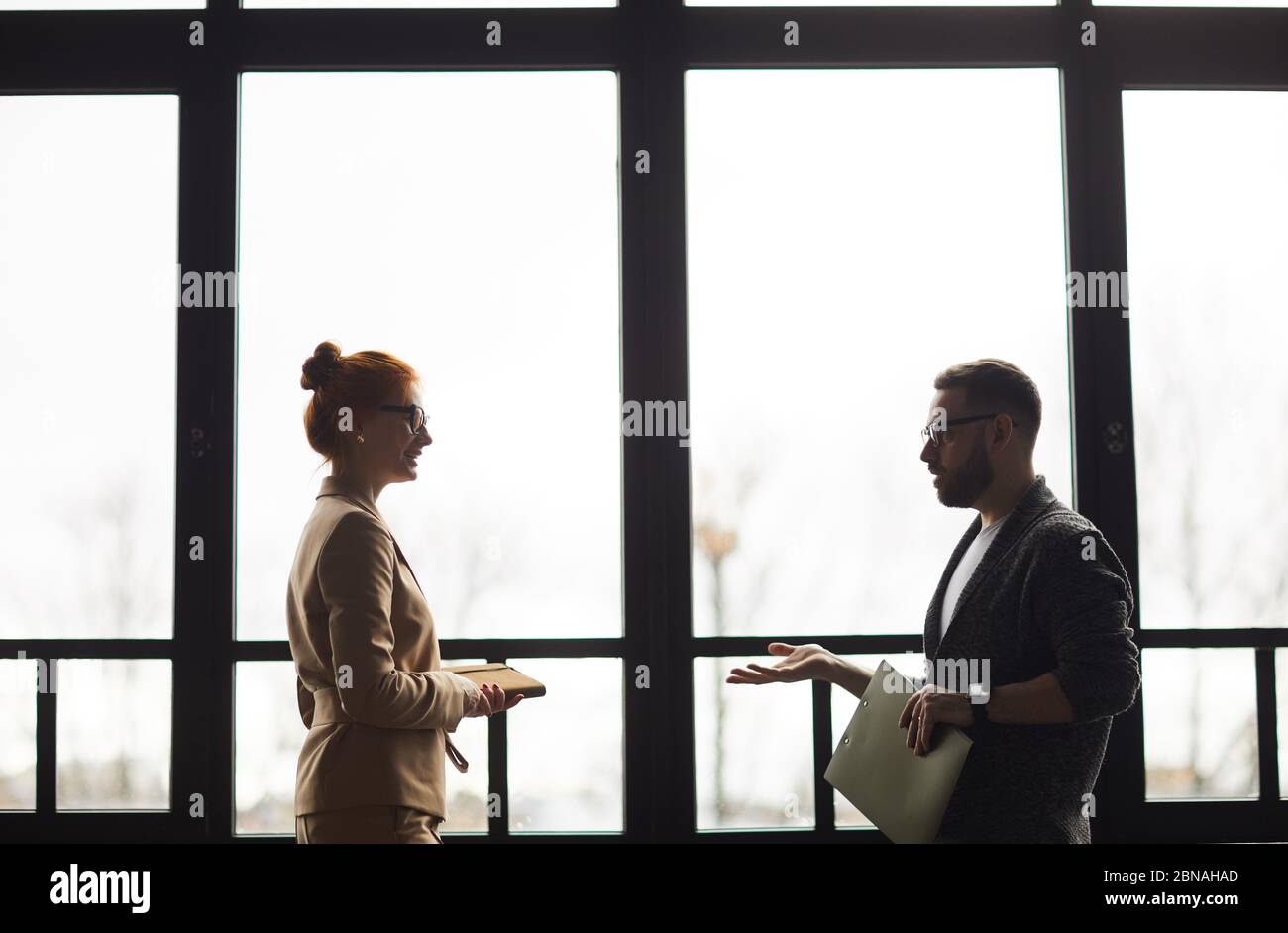 Two business partners talking to each other while standing in front of ...