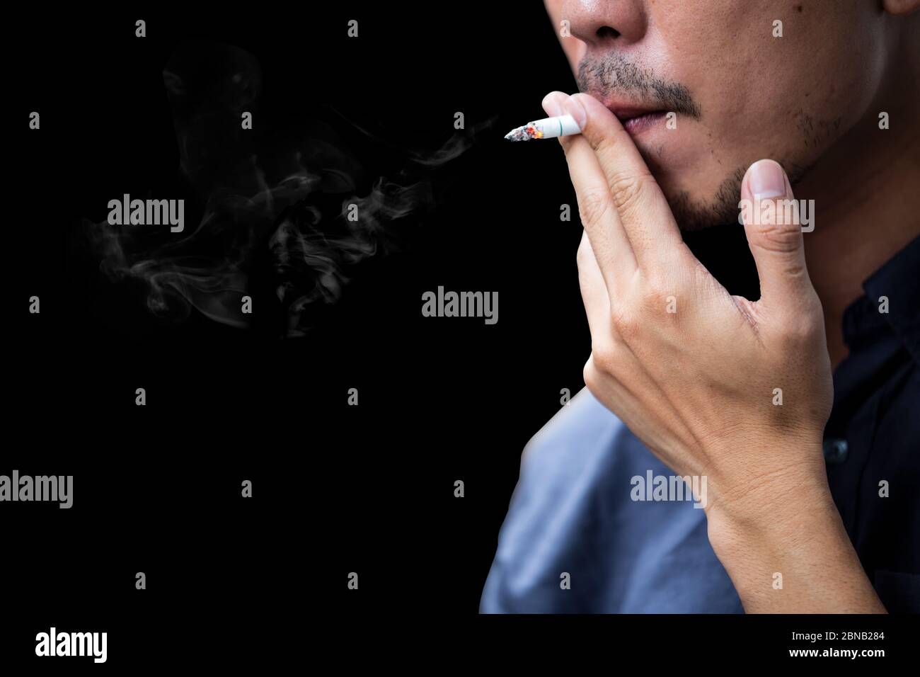 Side view of young bearded man smoking cigarette on black background ...