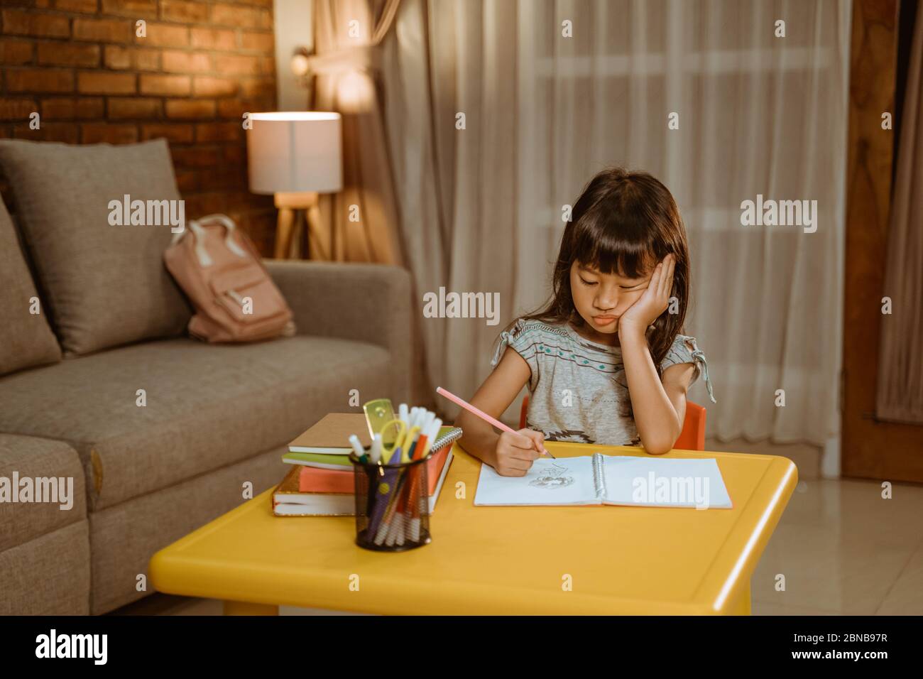 kid feel bored while doing her homework at home in the evening Stock ...