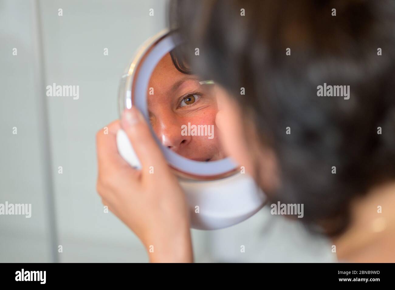 Woman plucking her eyebrows using a small handheld portable mirror in ...