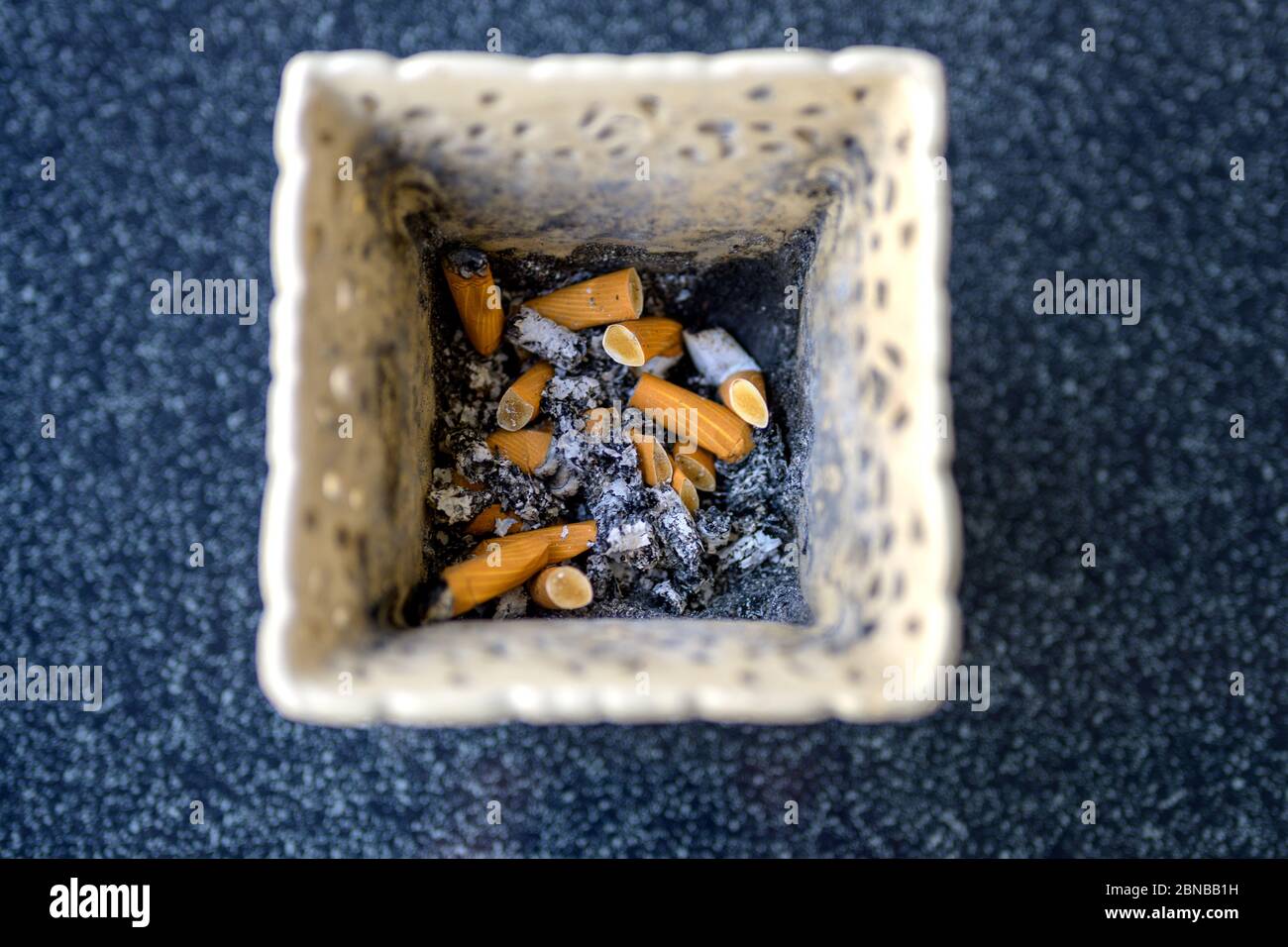 Old discarded cigarette stubs and ash in a bin viewed from overhead ...