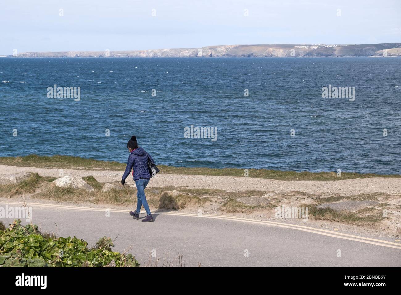 A woman walking along a road overlooking Watergate Bay in Cornwall ...