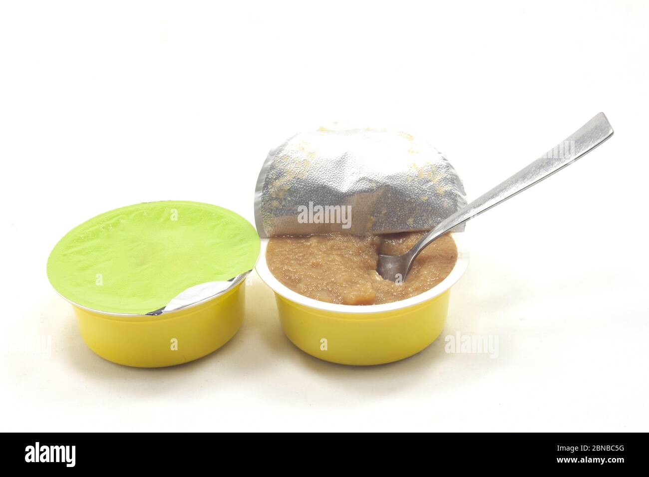 Apple custard with a spoon in a yellow plastic cup and a white ...