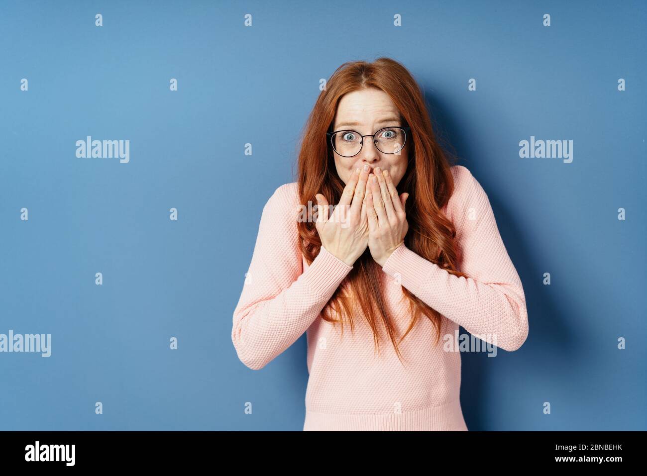 Young woman trying to stifle a laugh as she stares wide eyed at the ...