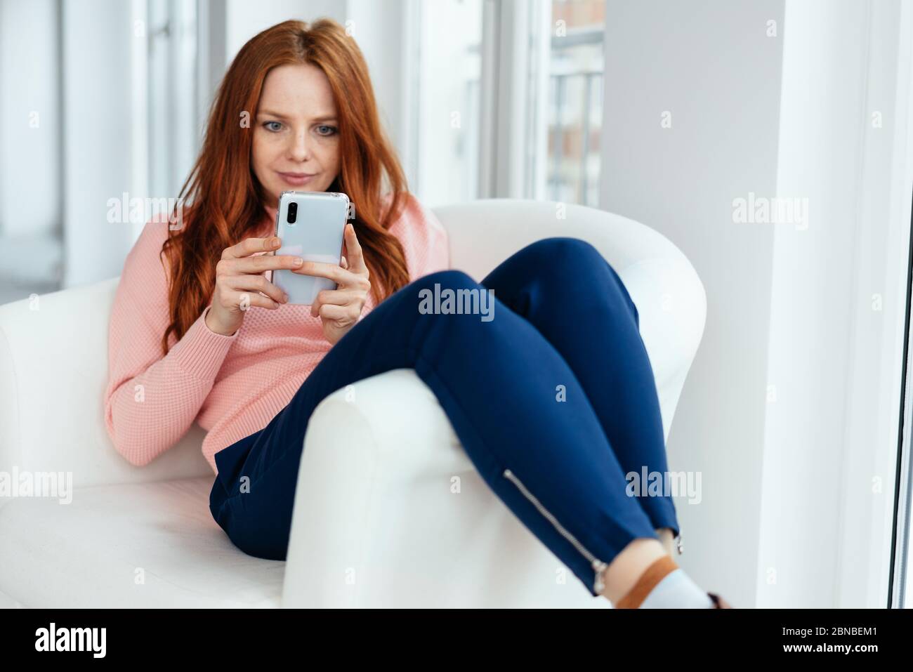 Engrossed young woman reading a text message on her mobile phone as she ...