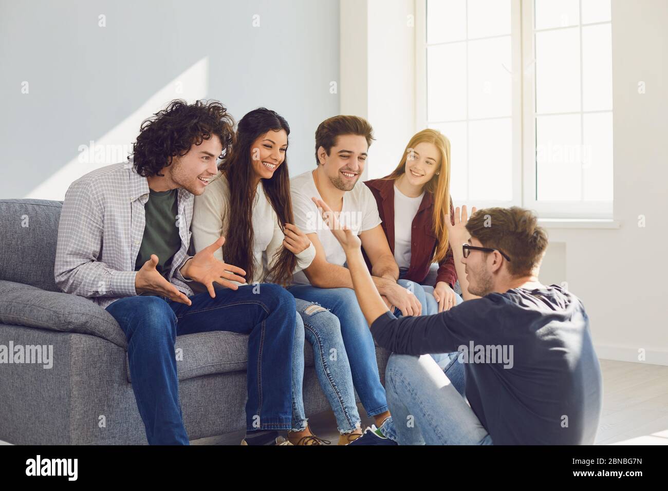 A group of friends is sitting on the couch in a room on a gray ...