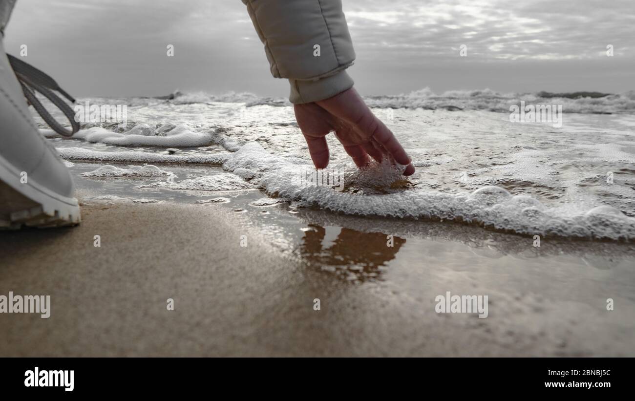Person with her hand in the waves on the beach captured at daylight ...