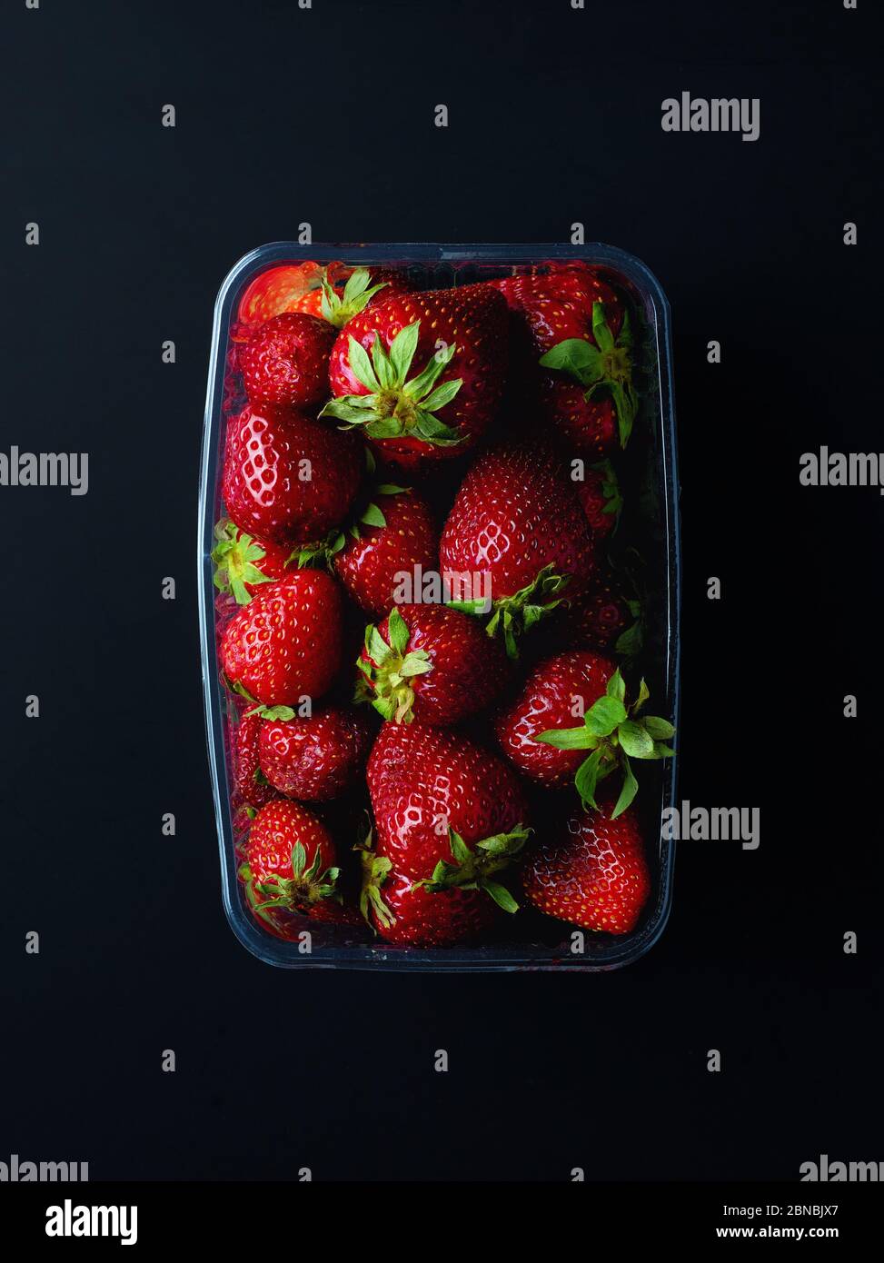 Strawberries in plastic transparent container box on black background ...