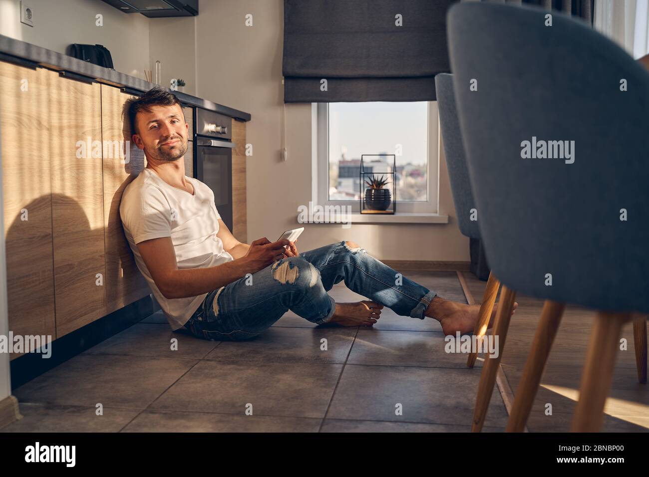 Thinking man sitting on floor using laptop and smiling against clouds ...