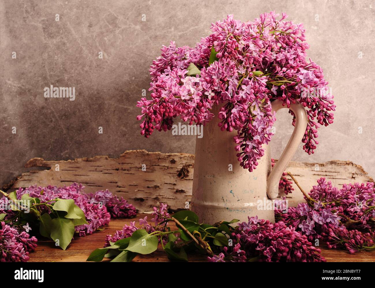 Horizontal photo of purple lilacs in old worn ceramic pitcher. Concrete ...