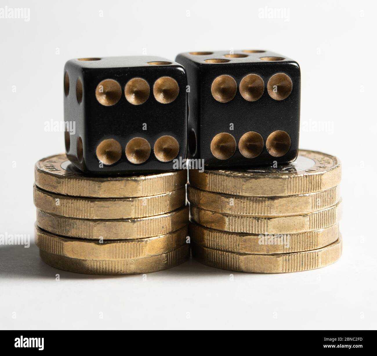 Two black dice on stacks of one pound coins against a white background ...