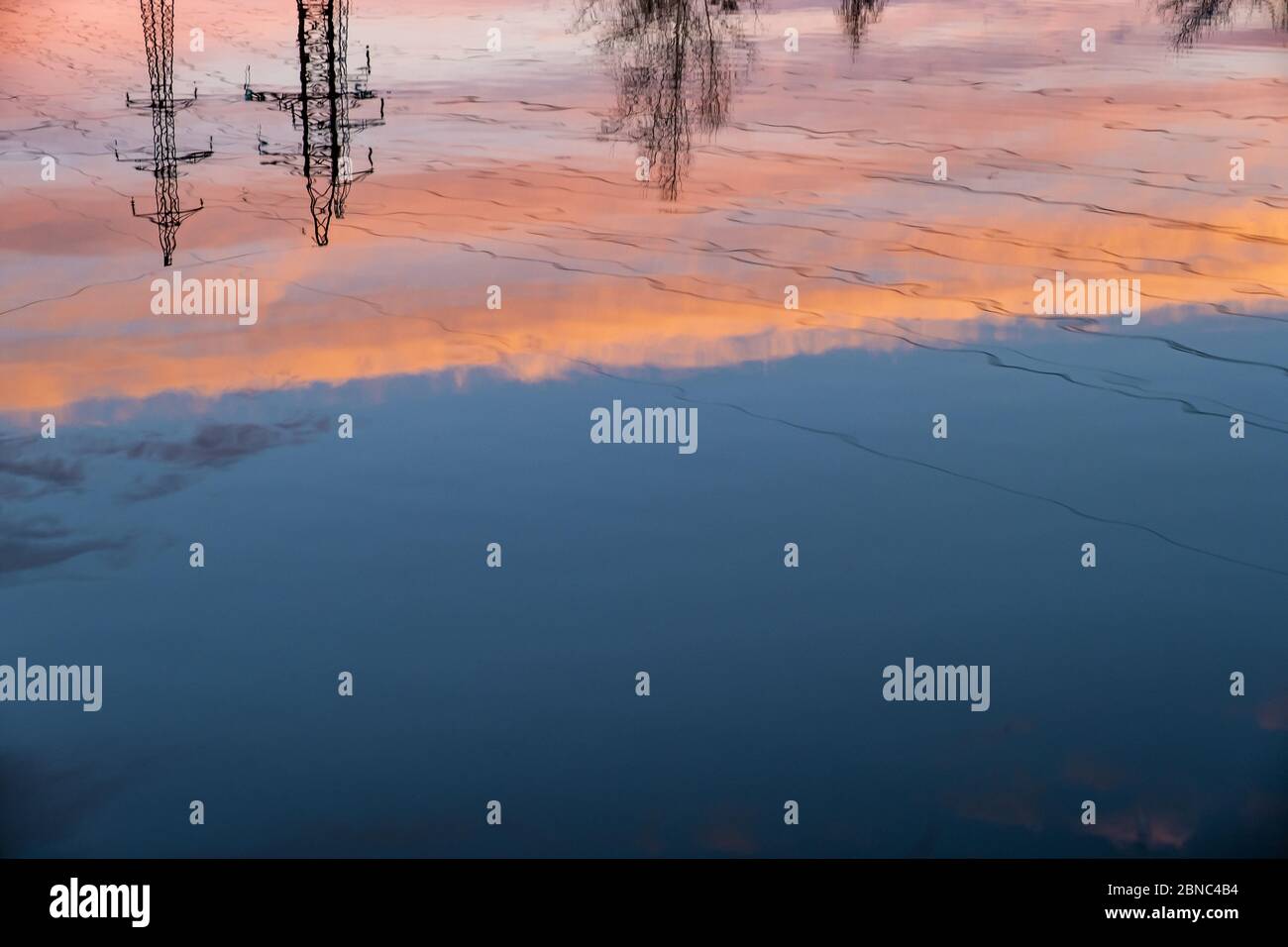 Reflection of the power line pylon and orange sunset clouds in the ...