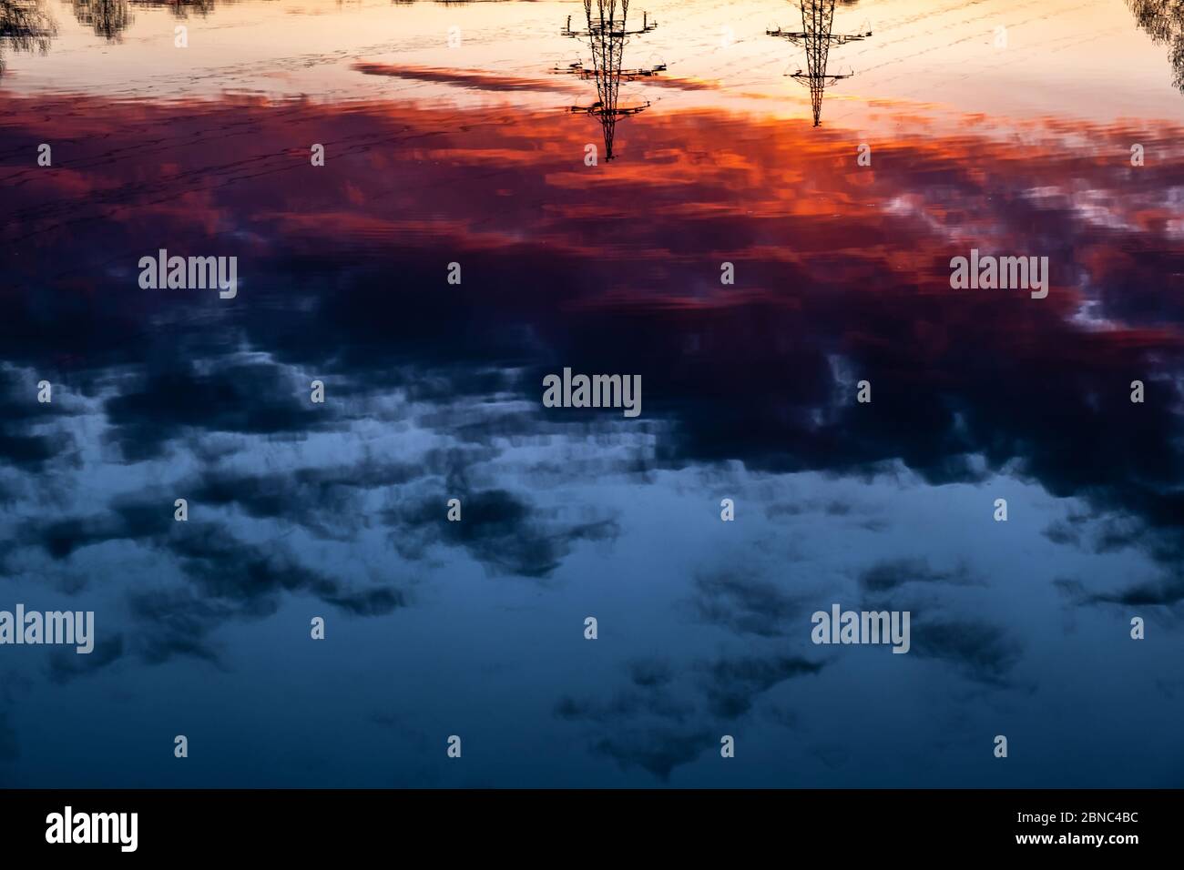 Reflection of the power line pylon and orange sunset clouds in the ...