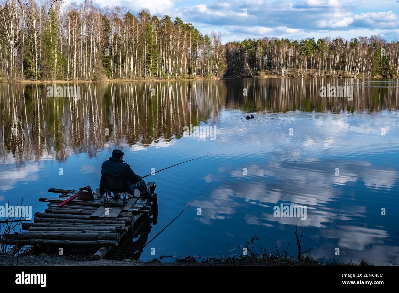 Fisherman on a log pier against the background of the forest and a ...