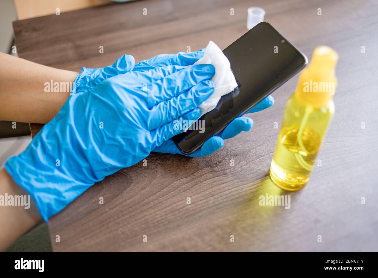 Woman's hand in blue gloves sanitizing cleaning smartphone mobile phone ...