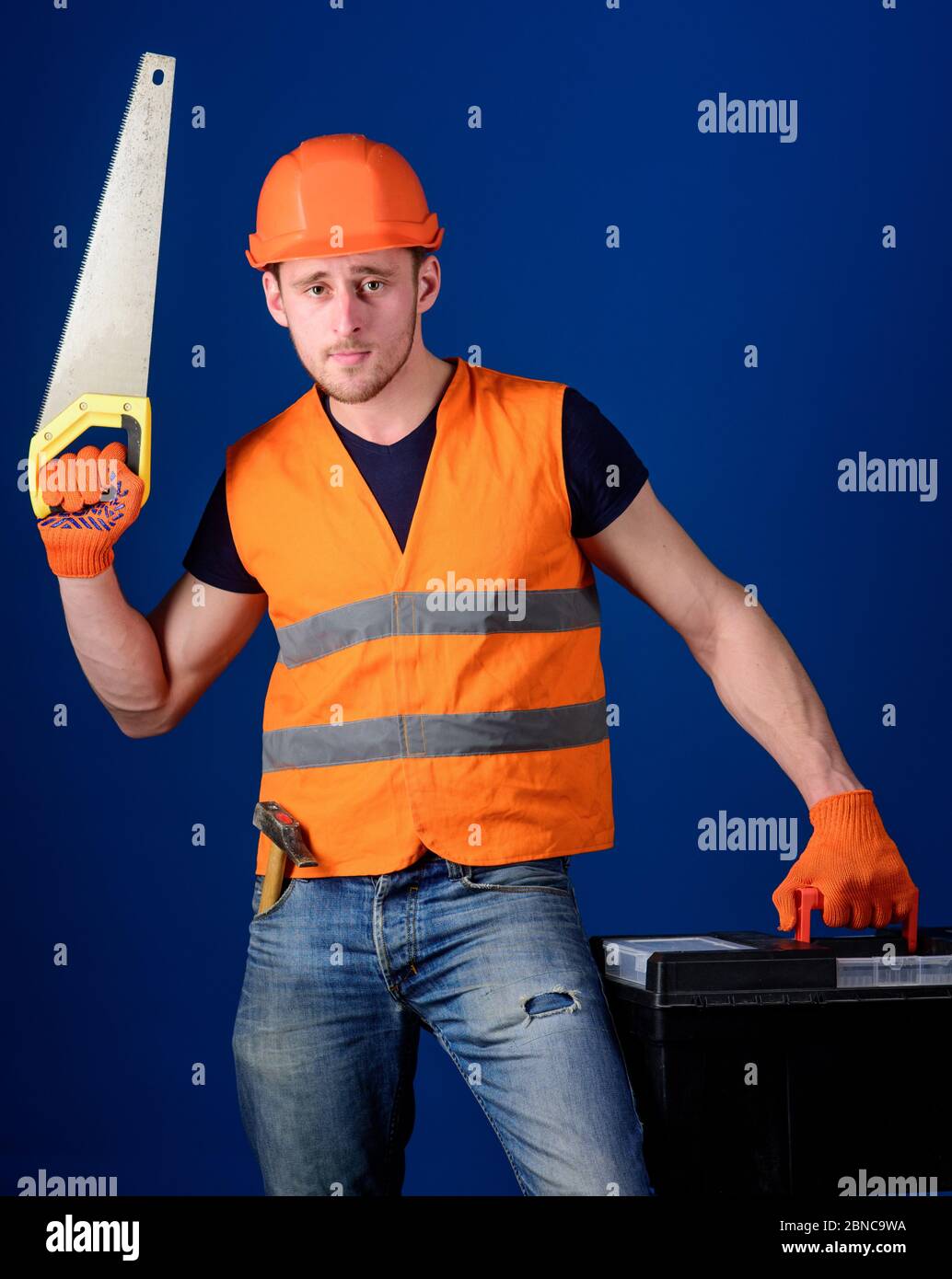 Man in helmet, hard hat carries toolbox and holds handsaw, blue ...
