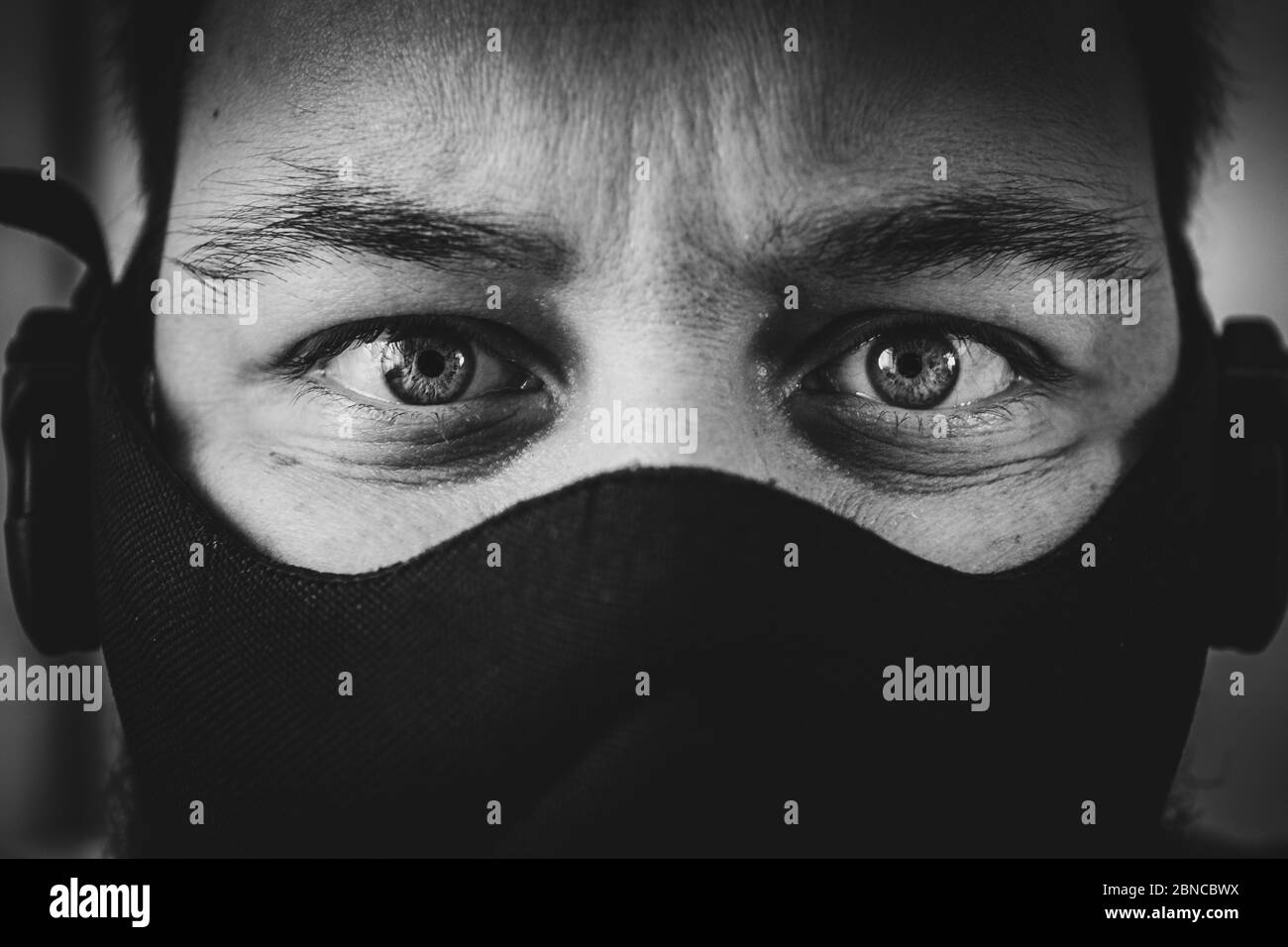 Greyscale shallow shot of a male's face wearing a mask staring directly ...
