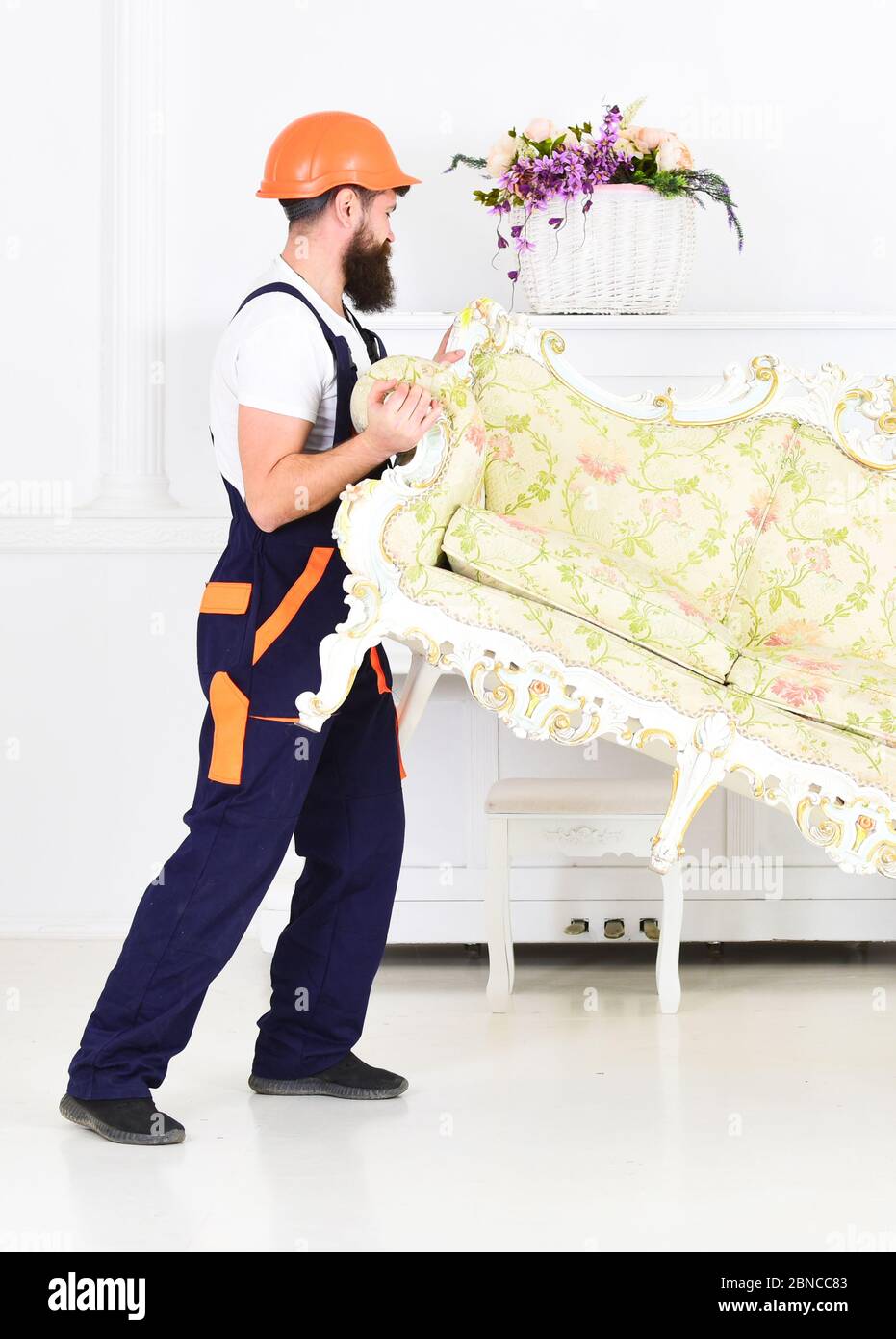 Loader moves sofa, couch. Man with beard, worker in overalls and helmet ...