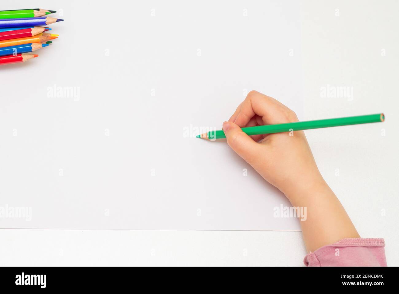 Top view of kid's hand drawing on the white paper with pencils. Concept ...
