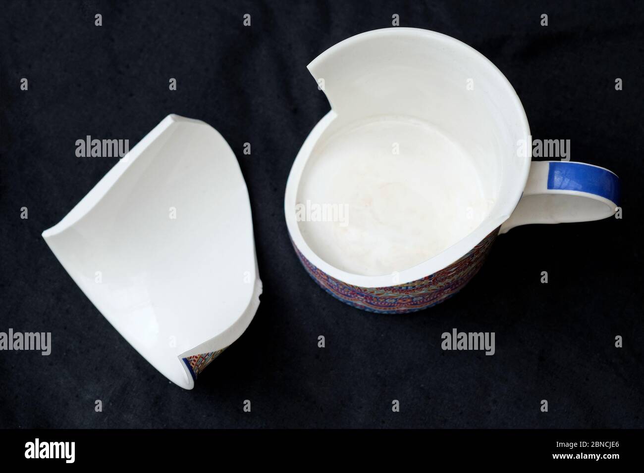 Broken ceramic cup on a black background. Two parts of a white cup with ...