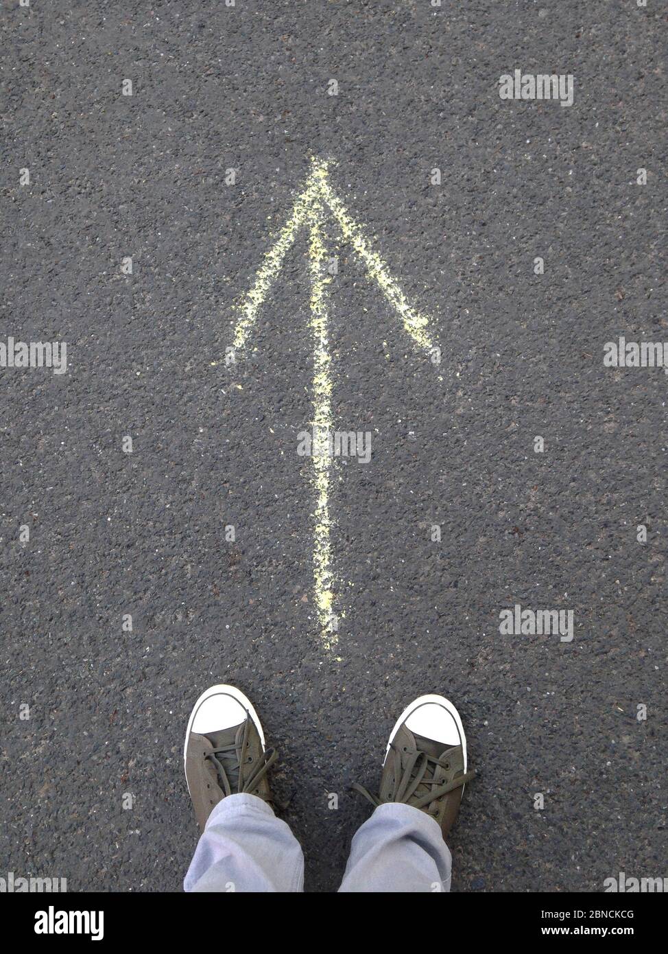 Vertical shot of a person's feet and an arrow on the ground pointing to ...