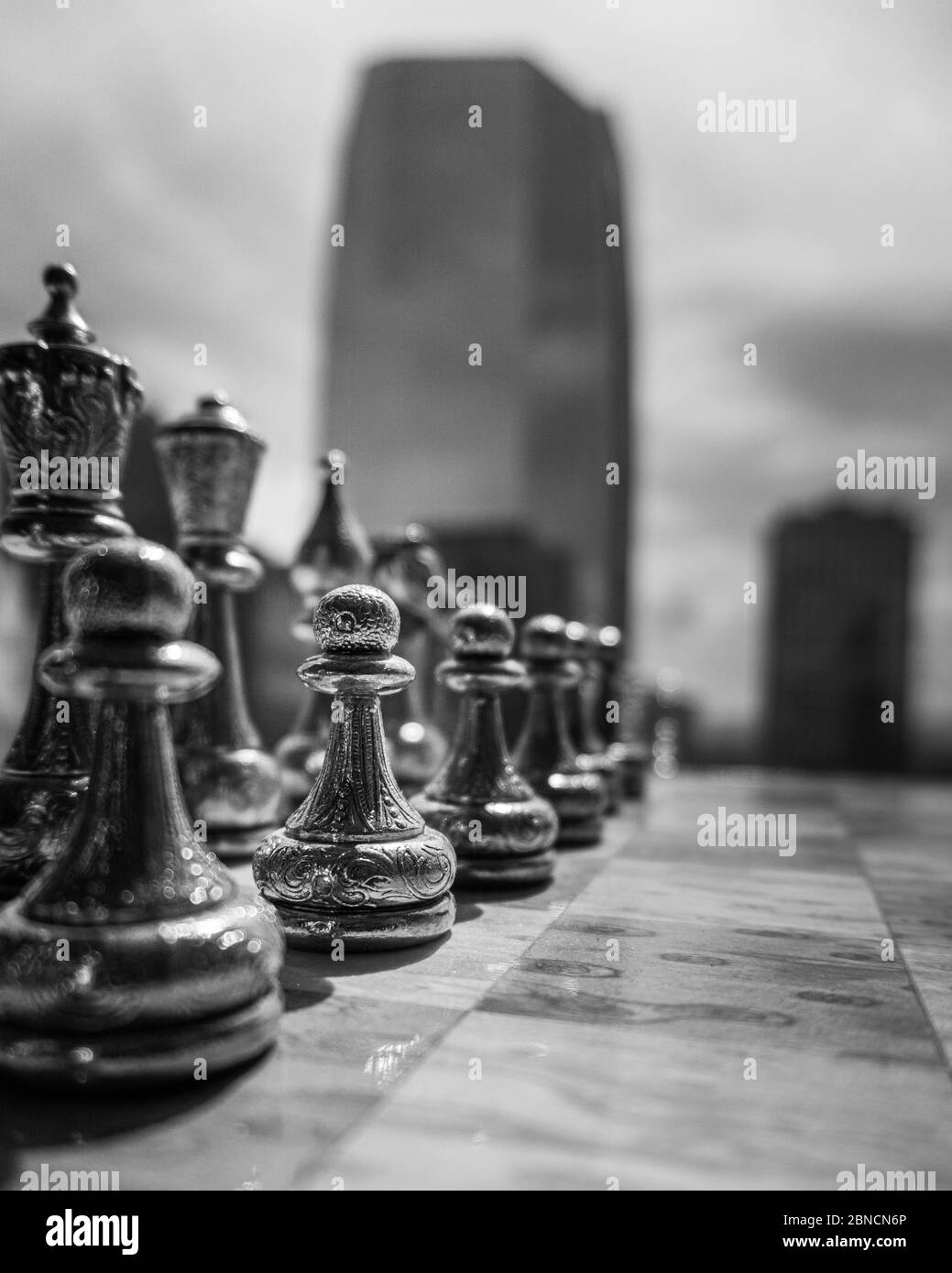 Vertical grayscale shot of chess figurines with buildings in the ...