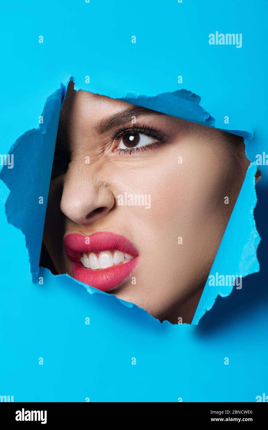 Aggressive woman with pink lips looking across ripped blue paper Stock ...