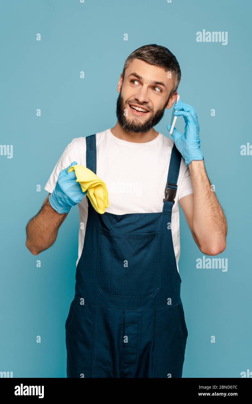 happy cleaner in uniform and rubber gloves with rug talking on ...