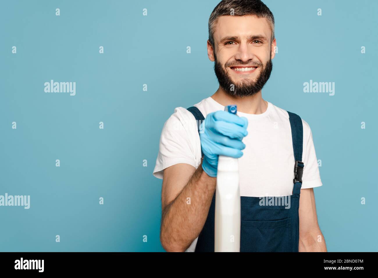 happy cleaner in uniform and rubber gloves holding spray detergent on ...