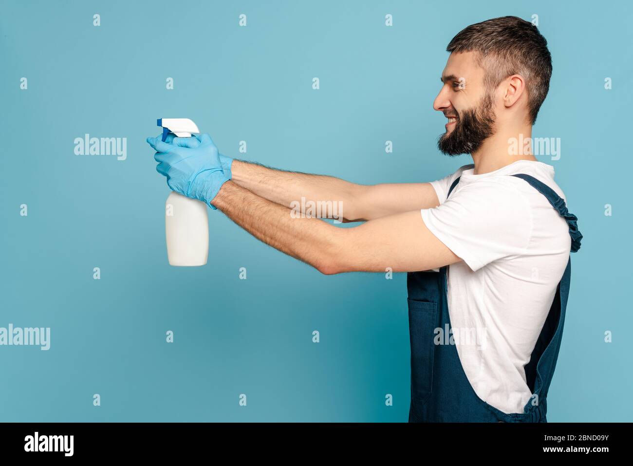 side view of happy cleaner in uniform and rubber gloves holding spray ...