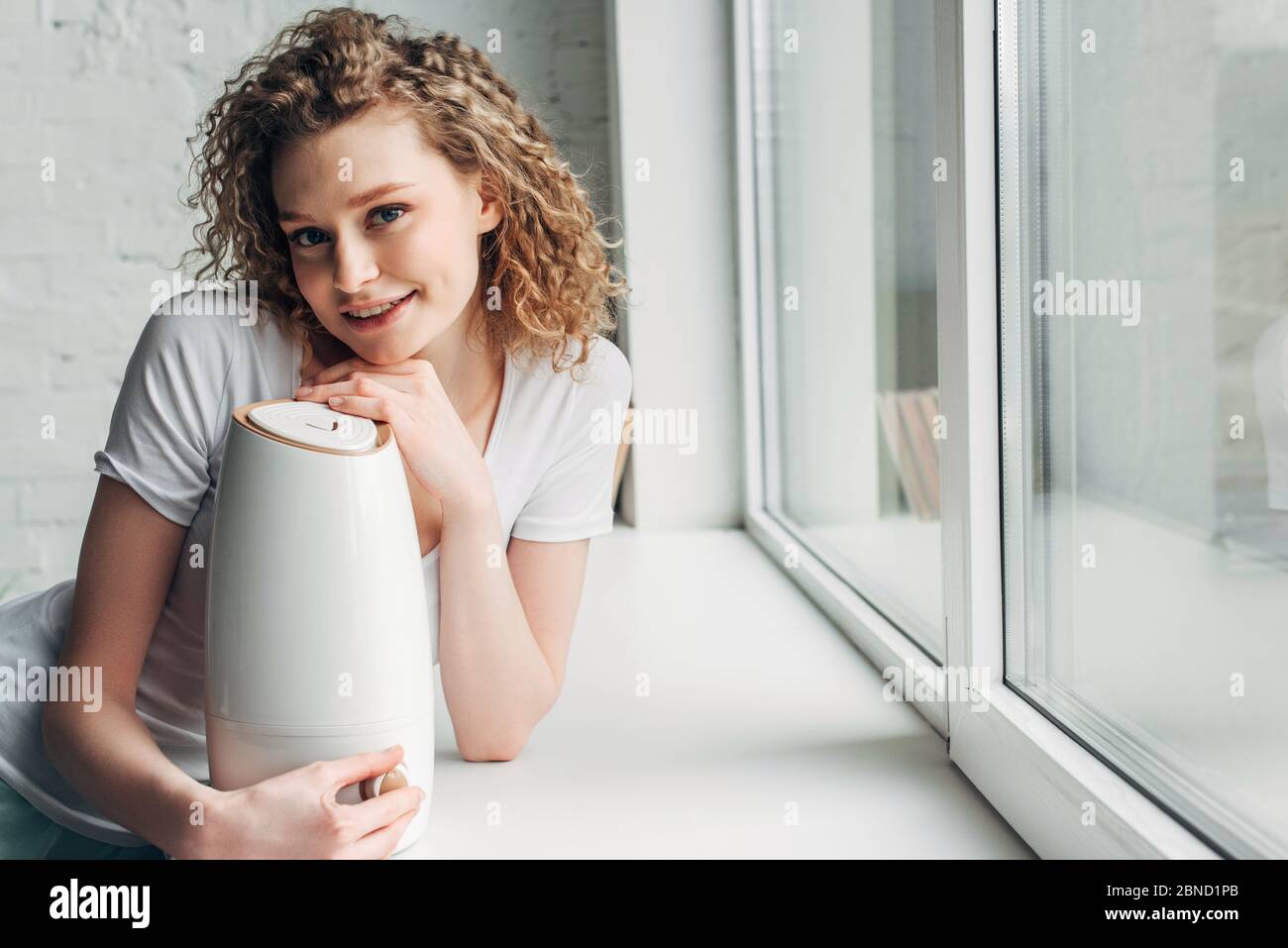 attractive smiling girl with air purifier on windowsill Stock Photo - Alamy