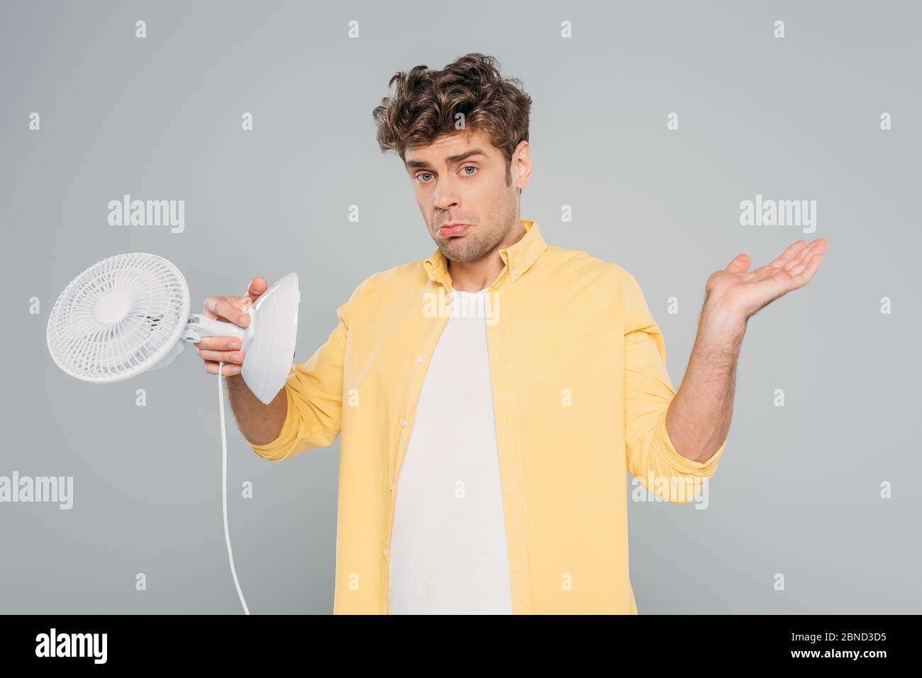 Front view of confused man holding desk fan and looking at camera ...