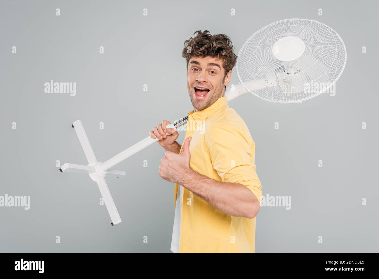Excited man with open mouth holding electric fan, looking at camera and ...