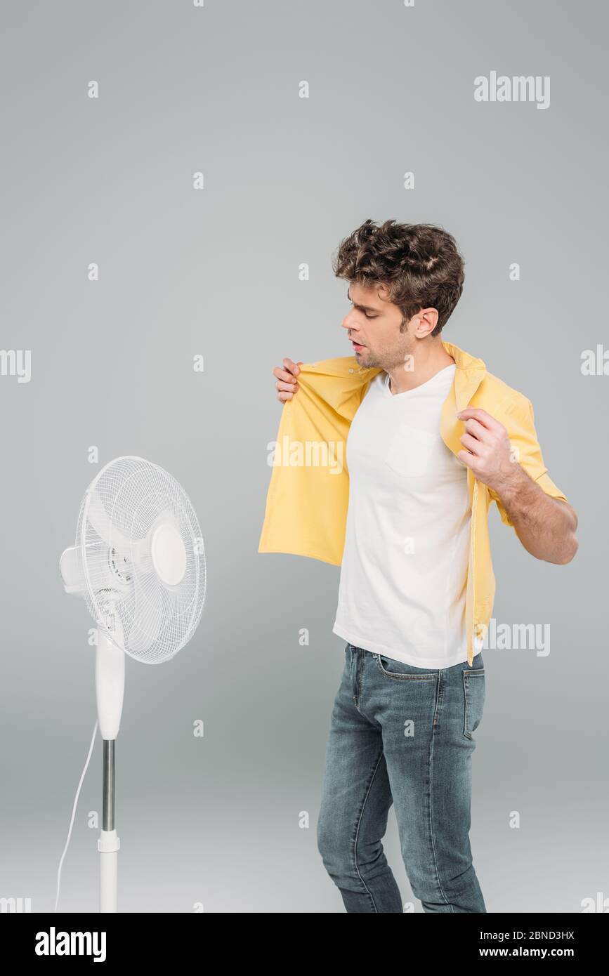 Man touching shirt in front of electric fan isolated on grey Stock ...