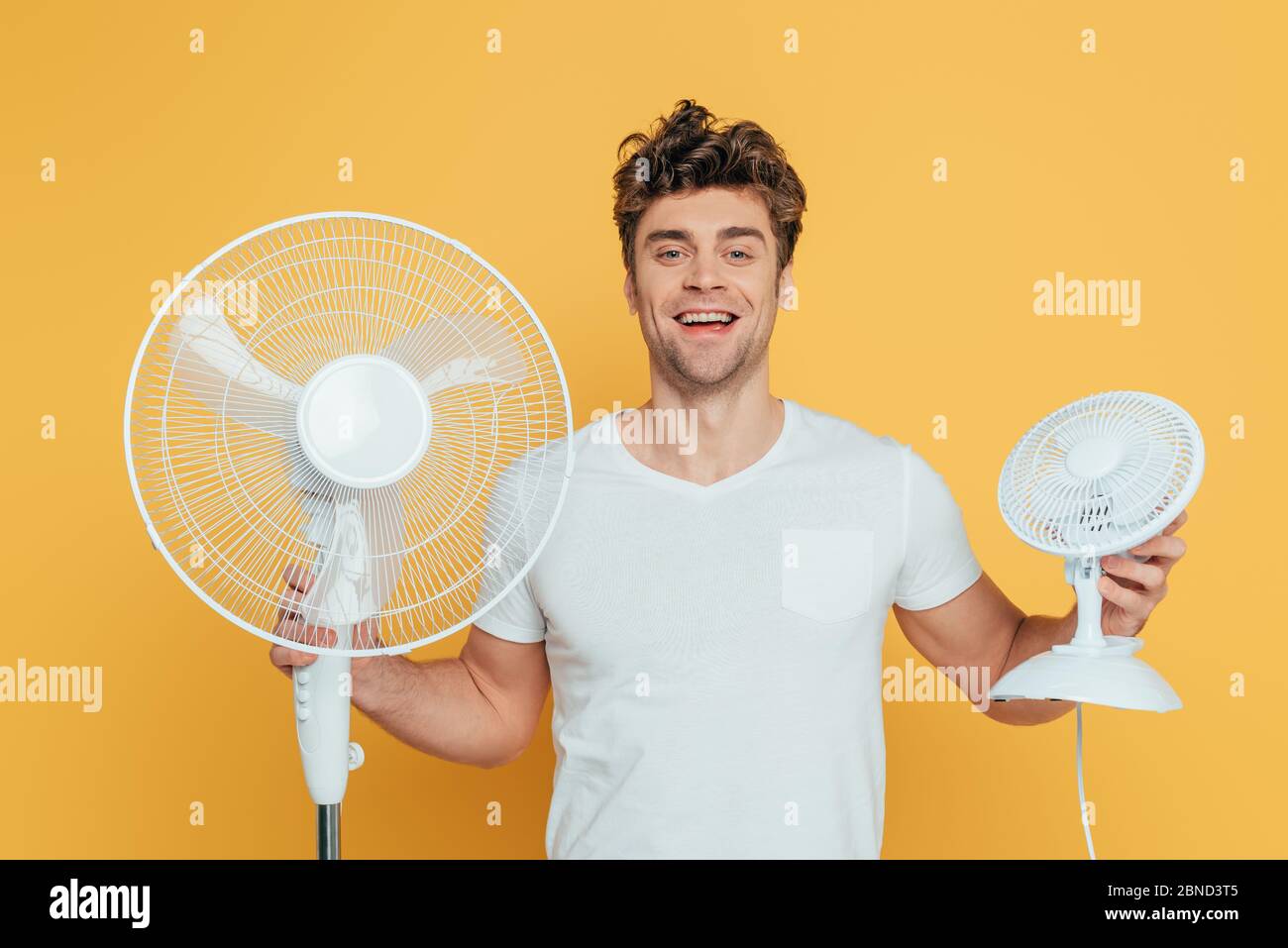 Front view of man holding electric and desk fans, smiling and looking ...