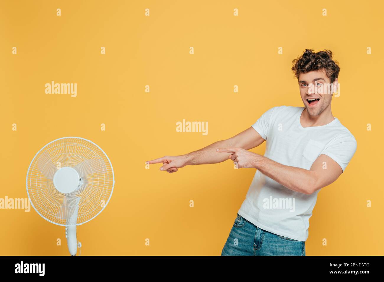 Excited man looking at camera and pointing at electric fan isolated on ...