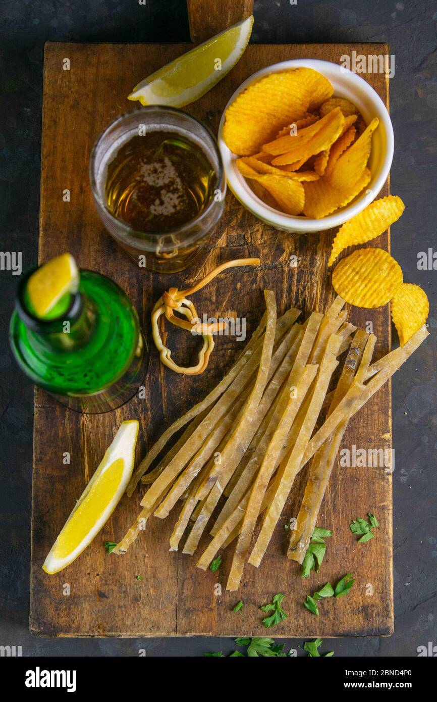 Dried salted tuna elite snack with beer, lemon and potato chips on dark ...