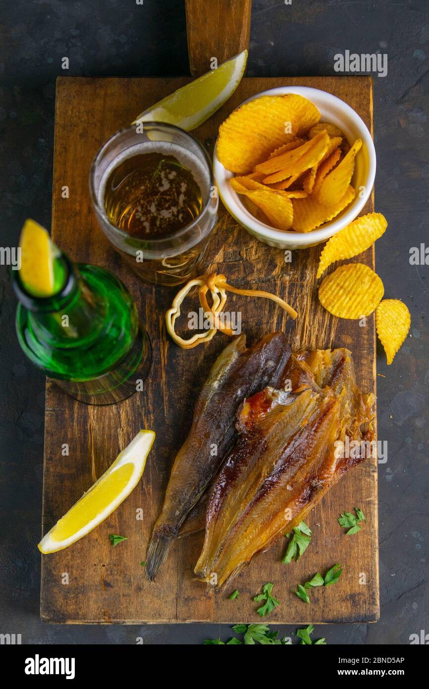 Dried blue whiting fish with beer, lemon and potato chips on dark ...