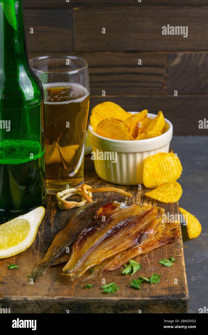 Dried blue whiting fish with beer, lemon and potato chips on dark ...